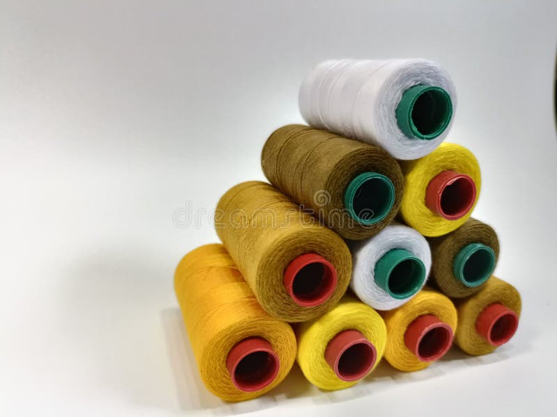 Pyramid Stack of Yellow, White, and Brown Sewing Thread Spools on White ...