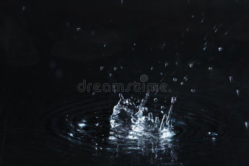 Rain Drop Falling Down into Puddle on Dark Background Stock Photo ...
