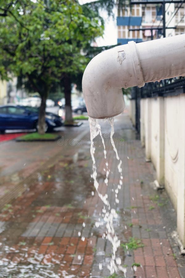 Rain Water is Pouring from the White Draining Gutter on the Pavement ...