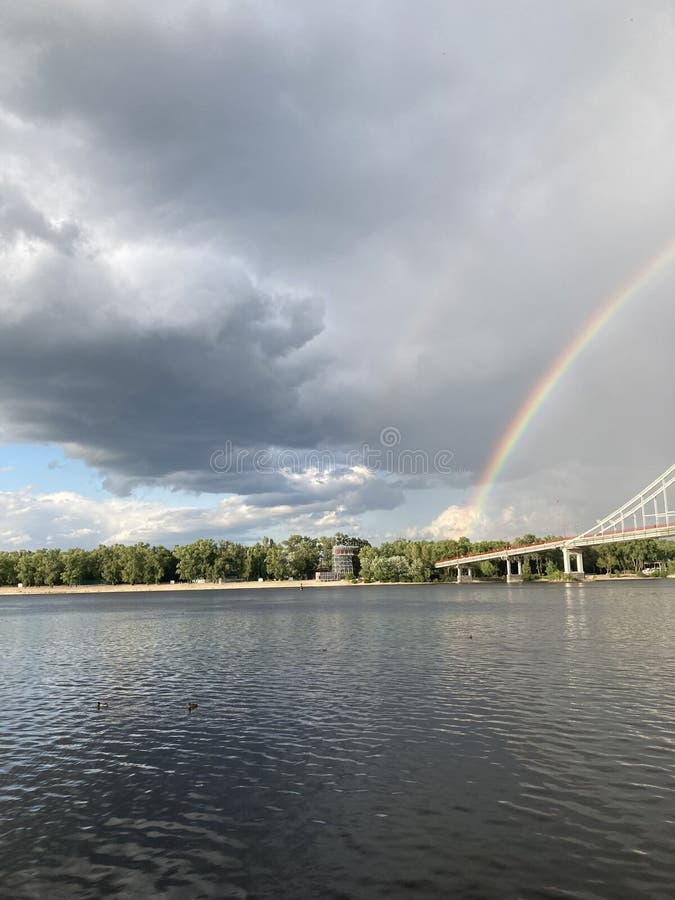 A Rainbow Arches Over a Tranquil Body of Water, Reflected Below the ...
