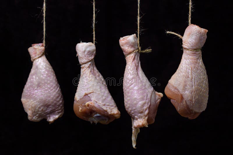Raw Chicken Legs on a Black Background. Chicken Legs Hang Suspended by ...