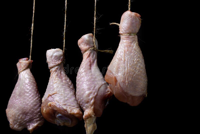 Raw Chicken Legs on a Black Background. Chicken Legs Hang Suspended by ...