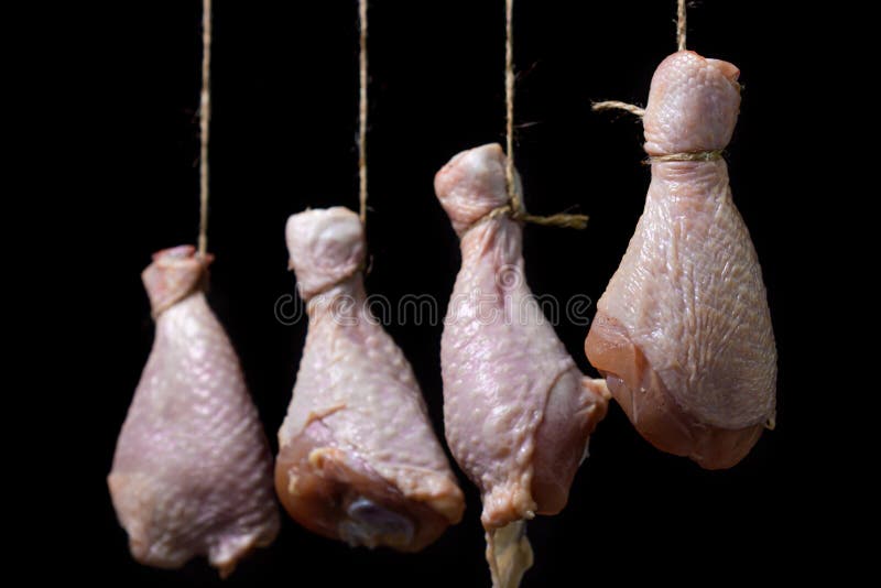 Raw Chicken Legs on a Black Background. Chicken Legs Hang Suspended by ...