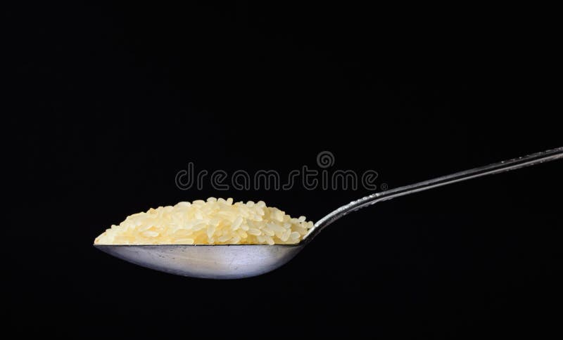 Raw Rice Poured into a Silver Spoon. Side View on a Black Background ...