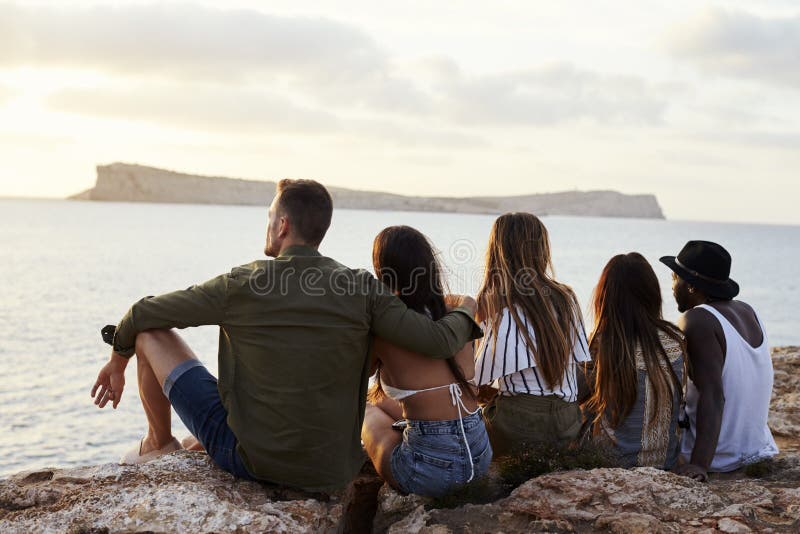 Side View of Couple Sitting on Cliff Watching Sunset Stock Photo ...