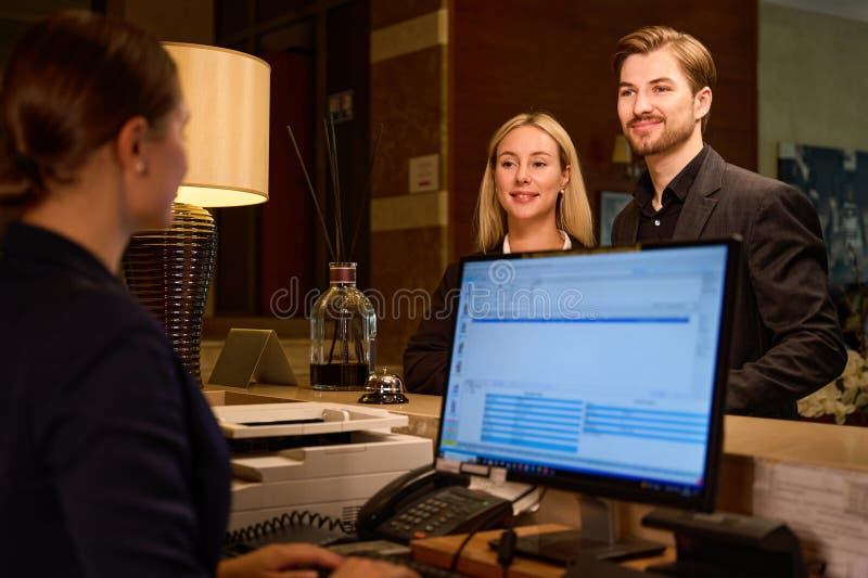 Receptionist Typing on Computer while Couple Standing at Reception Desk ...