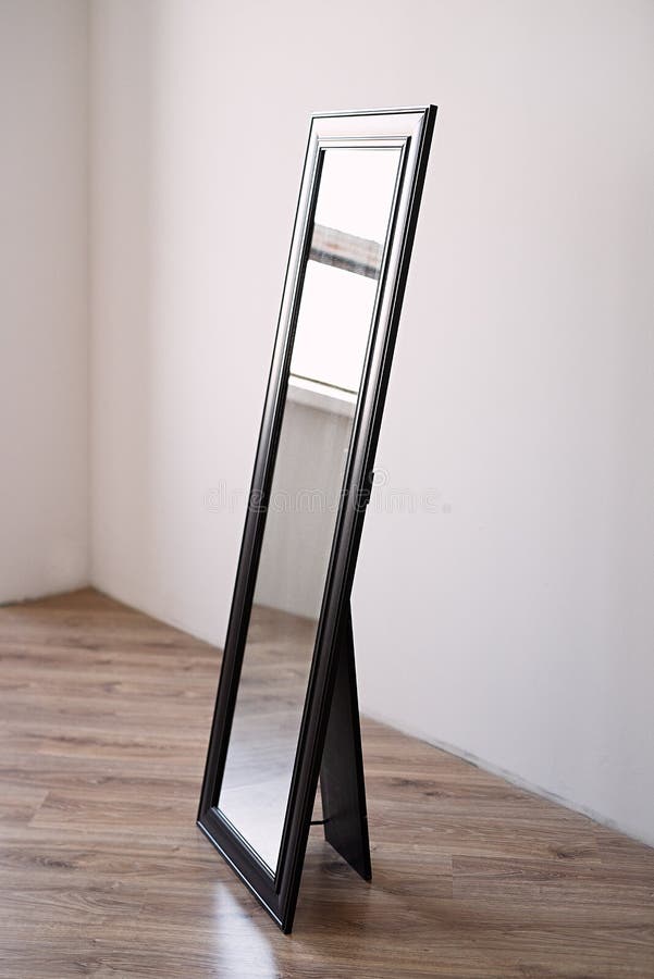 A Rectangular Mirror in a Brown Wooden Frame Stands Indoors on a White ...
