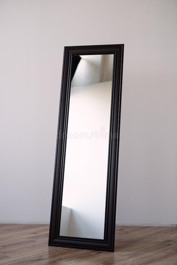 A Rectangular Mirror in a Brown Wooden Frame Stands Indoors on a White ...