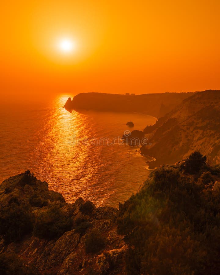 A Red Burning Sunset with the Silhouett of a Cliff Over the Sea Stock ...