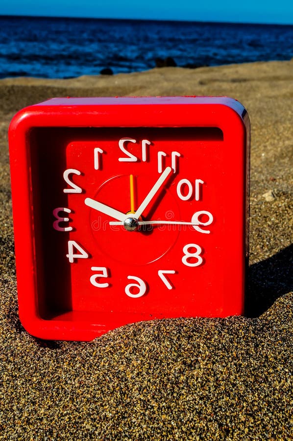 A Red Clock with the Numbers 1 To 12 on it is Sitting on a Sandy Beach ...