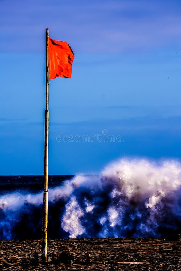 A Red Flag is on a Pole in Front of a Large Wave Stock Image - Image of ...
