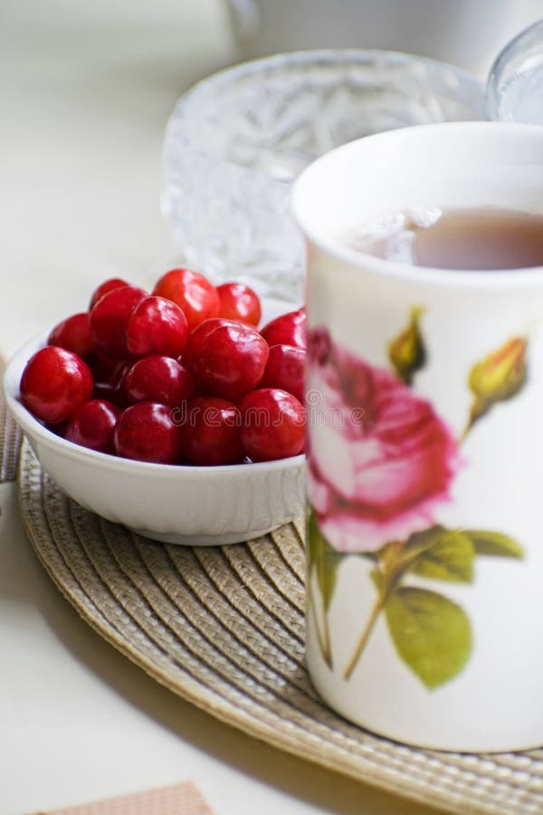 Red Juicy and Ripe Cherries in a White Bowl and a Cup of Tea on a Table ...