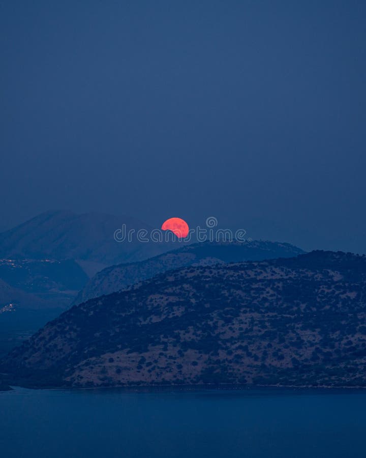 Red Moon Rising Over Dark Mountains and Serene Waters Stock Image ...