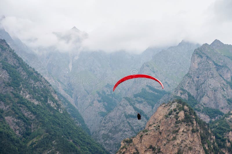 Red Paraglider Flies Against the Background of Mountains and Clouds ...
