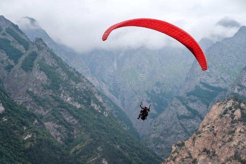 Red Paraglider Flies Against the Background of Mountains and Clouds ...