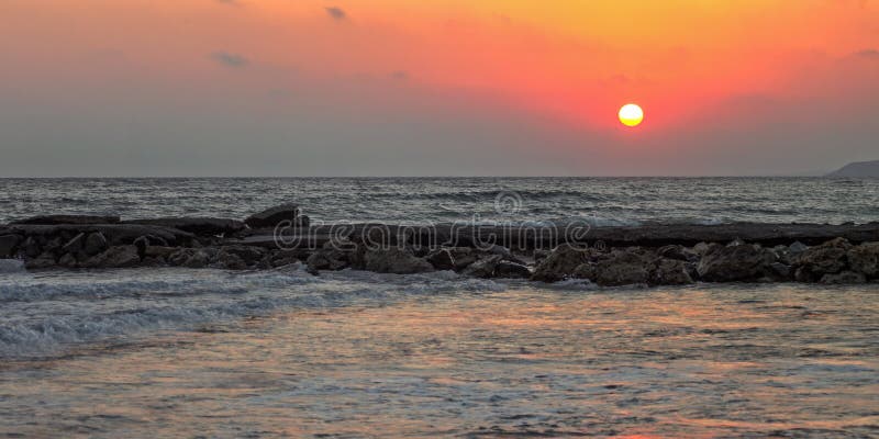 Red Setting Sun Over Calm Sea, Line of Rocks in Foreground. Stock Photo ...