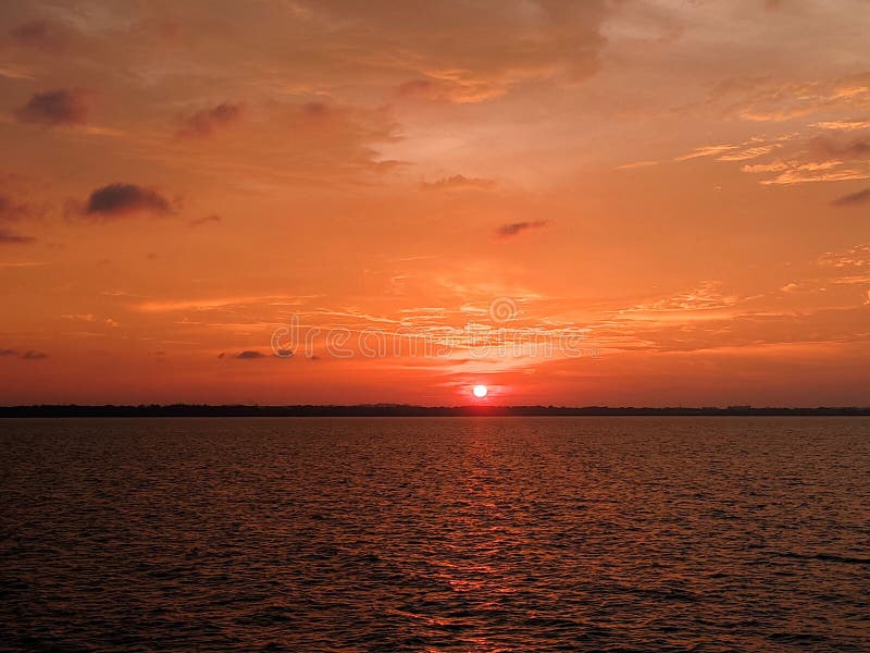 A Red Sun Setting Over the Ocean with Clouds in the Sky Stock Photo ...