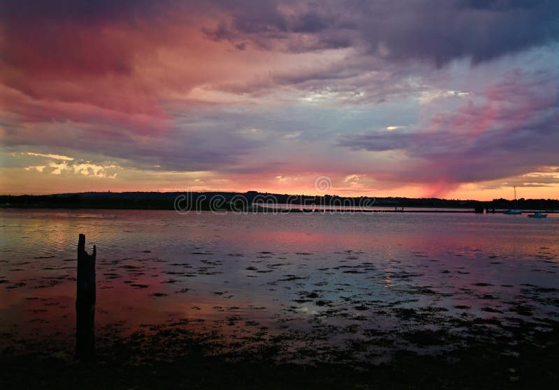 Red Sunset with Rain Clouds Over Water and Land in the Distance Stock ...