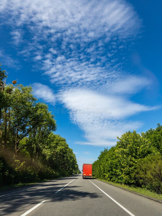 A Red Truck Driving Down a Road with Trees on Both Sides Stock Image ...
