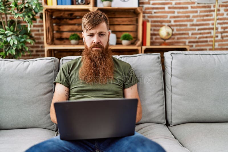 Redhead Man with Long Beard Using Laptop Sitting on the Sofa at the ...