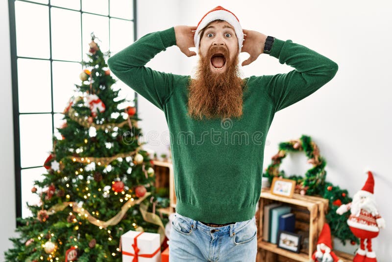 Redhead Man With Long Beard Wearing Christmas Hat By Christmas Tree