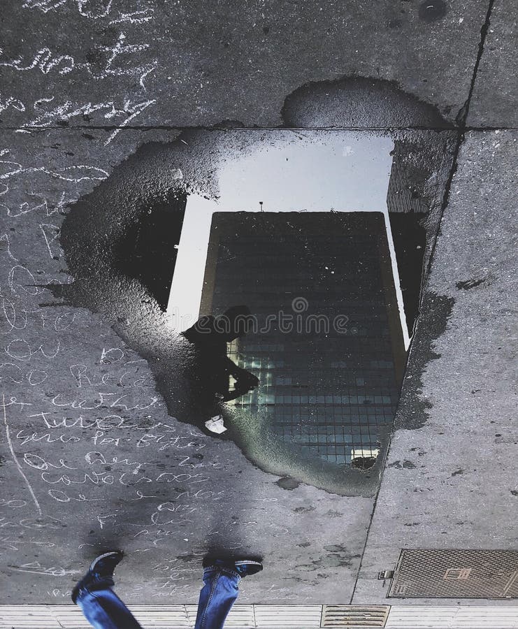 Reflection of a Man and a Modern Building on a Puddle of Water on ...