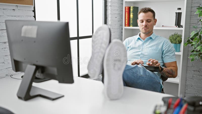 A Relaxed Hispanic Man with a Beard Lounges in an Office, Feet Up on ...