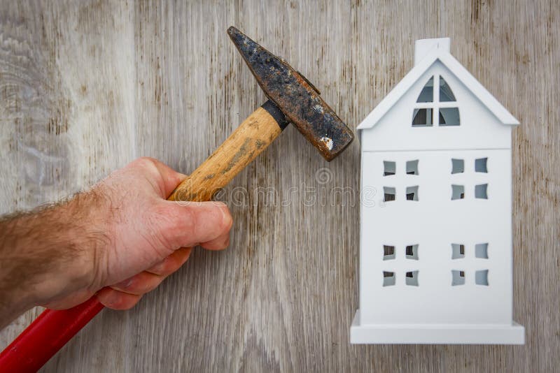 Repair House Concept. Hammer in Hand of Builder and Miniature Model of ...