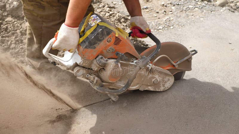 A Road Builder in Uniform Cuts Off the Old Asphalt with a Hand Grinder ...