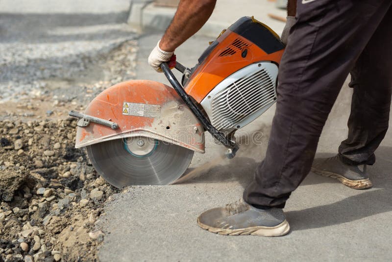 A Road Builder in Uniform Cuts Off the Old Asphalt with a Hand Grinder ...