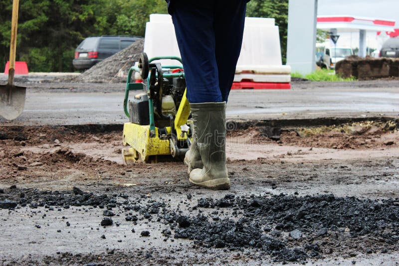 A Road Construction Worker Compacts the Soil with a Compact Vibroplate ...