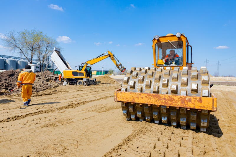 Road Roller with Spikes and Earthmover are Working at Construction Site ...