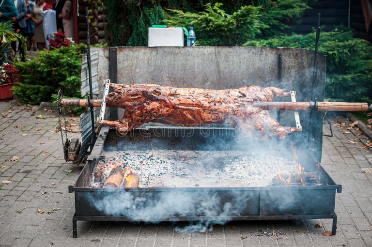 Roast Pig Spinning on a Grill Surrounded by Smoke and Greenery Stock ...