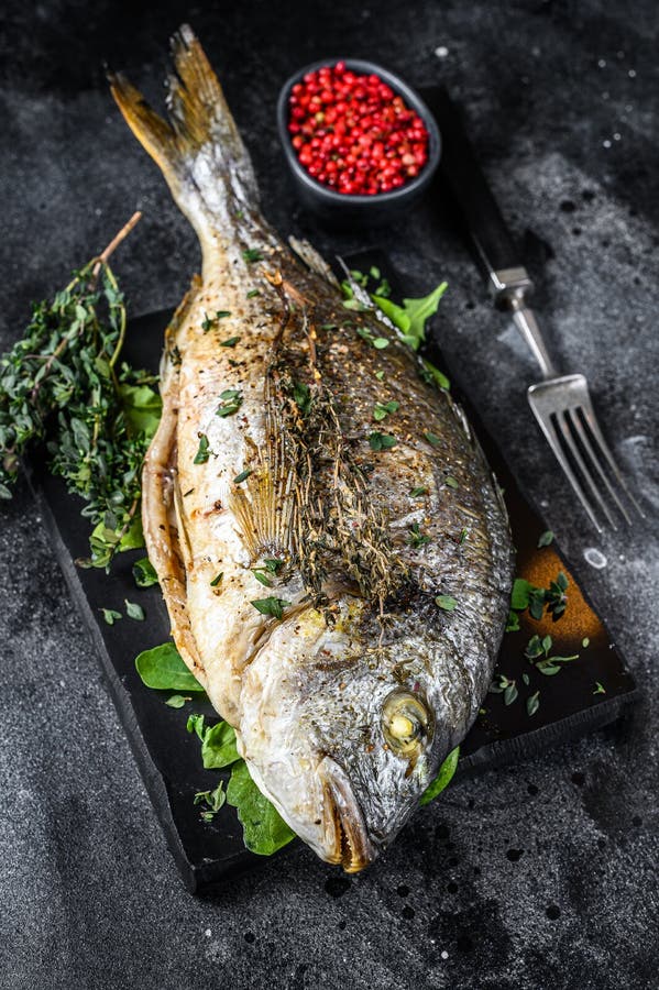 Roasted Sea Bream Fish with Herbs on a Cutting Board. Black Background ...