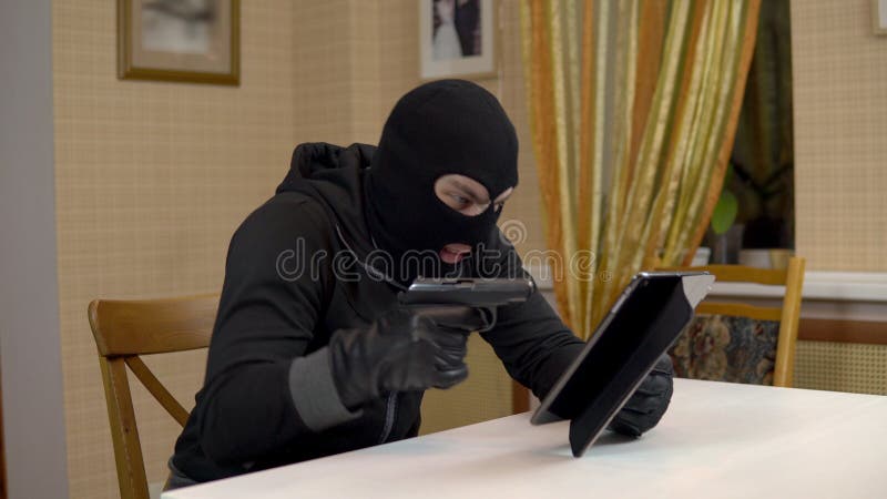 A Robber is Trying To Hack into a Tablet. a Masked Thug is Sitting in a ...