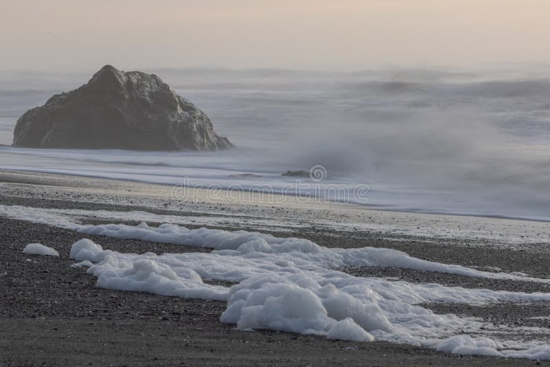 A Rocky Beach with a Large Rock and a Large Amount of Foam on the Shore ...