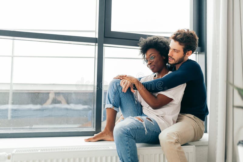 Romantic Mixed Race Couple Standing By The Window Thinking About Their