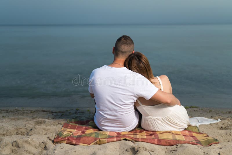 Romantic Portrait Of Couple In Love Hugs Sitting On The Beach At The