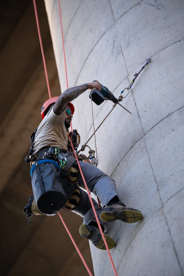 Rope Access Technician Using Drill while Hanging on Concrete Pillar ...