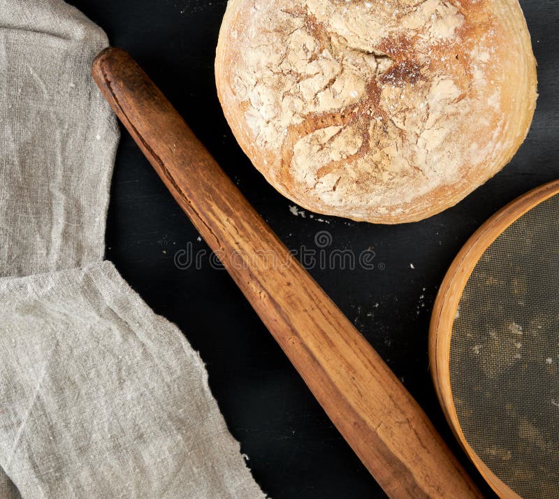 Round Baked Bread and Wooden Old Rolling Pin on a Black Table Stock ...