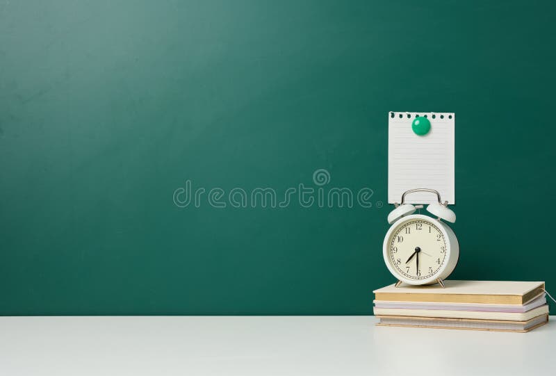 Round White Alarm Clock on a White Table, Behind an Empty Green ...