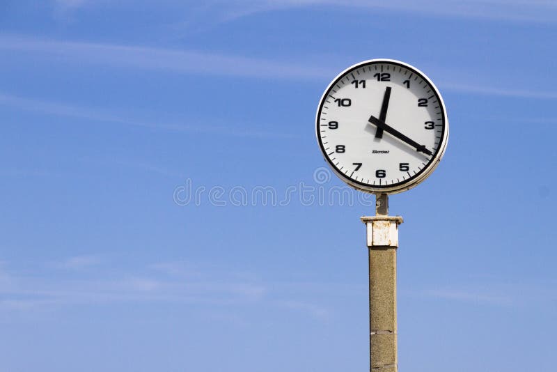 Round White Clock on a Concrete Post Against the Cloudy Blue Sky ...