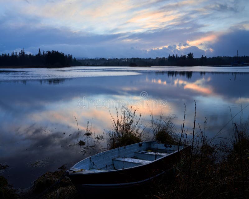 Silhouette of a Row Boat on the Shore at Dusk with Cloud Reflections in ...