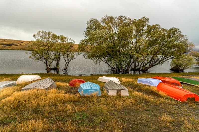 A Row of Colourful Upturned Rowing Boats Under the Trees on the Shore ...