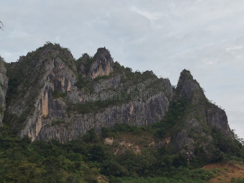 A Rugged Mountain Covered in Lush Greenery Rises Beneath a Cloudy Sky ...