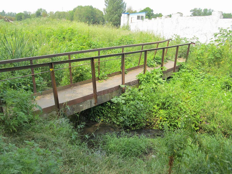 A Rustic Bridge Crosses Over a Stream or River Surrounded by Lush ...