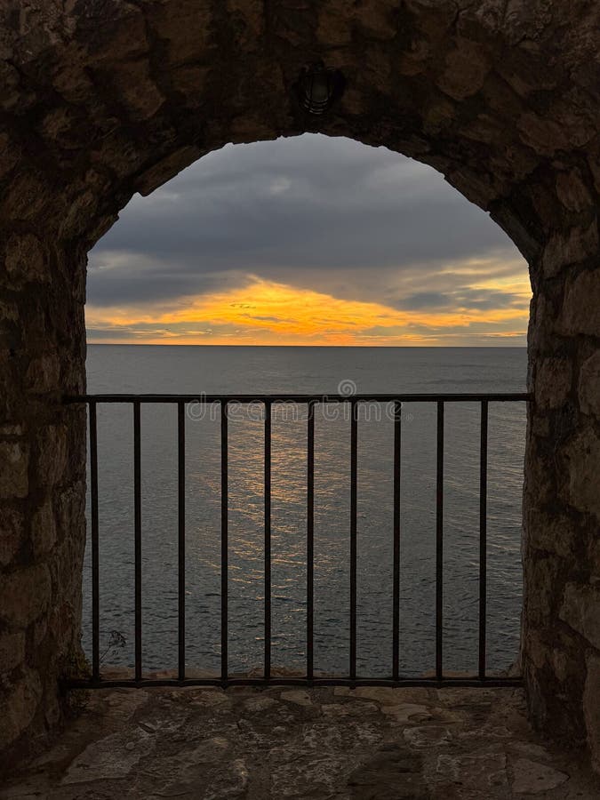 A Rustic Stone Archway Frames a View of Calm Blue Waters and a Golden ...