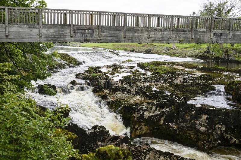 A Rustic Wooden Bridge Over a Cascading River Surrounded by Lush ...