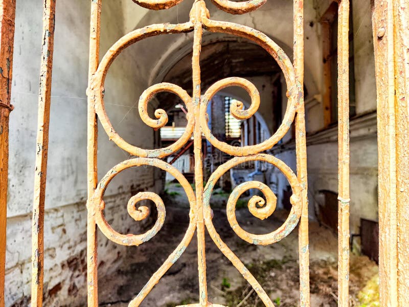 Rusty Gate with Intricate Scrollwork Leads into a Decaying Building ...