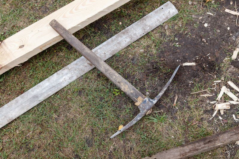 A Rusty Pickaxe is Laying on the Grass Next To a Wooden Plank Stock ...